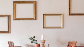 Uma sala de jantar com mesa e cadeiras de madeira, quadros nas paredes e um vaso com planta.