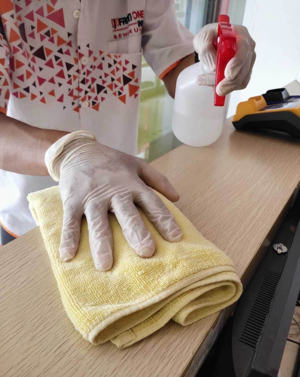 Uma pessoa limpando uma mesa de madeira com um pano amarelo e um borrifador.