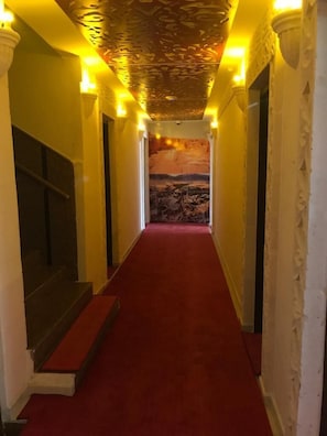Um corredor com carpete vermelho, paredes brancas e um mural de um pôr do sol.