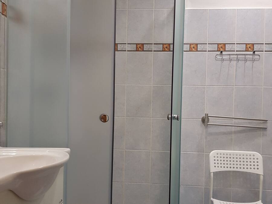 Casa de banho com cabine de chuveiro em vidro, pia branca, cadeira branca e paredes com azulejos.