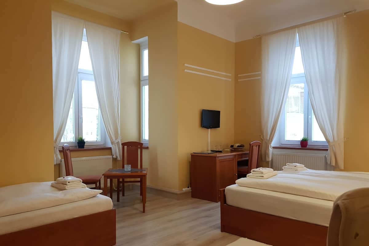 Quarto de hotel com duas camas, uma escrivaninha, uma cadeira, televisão e janelas com cortinas.
