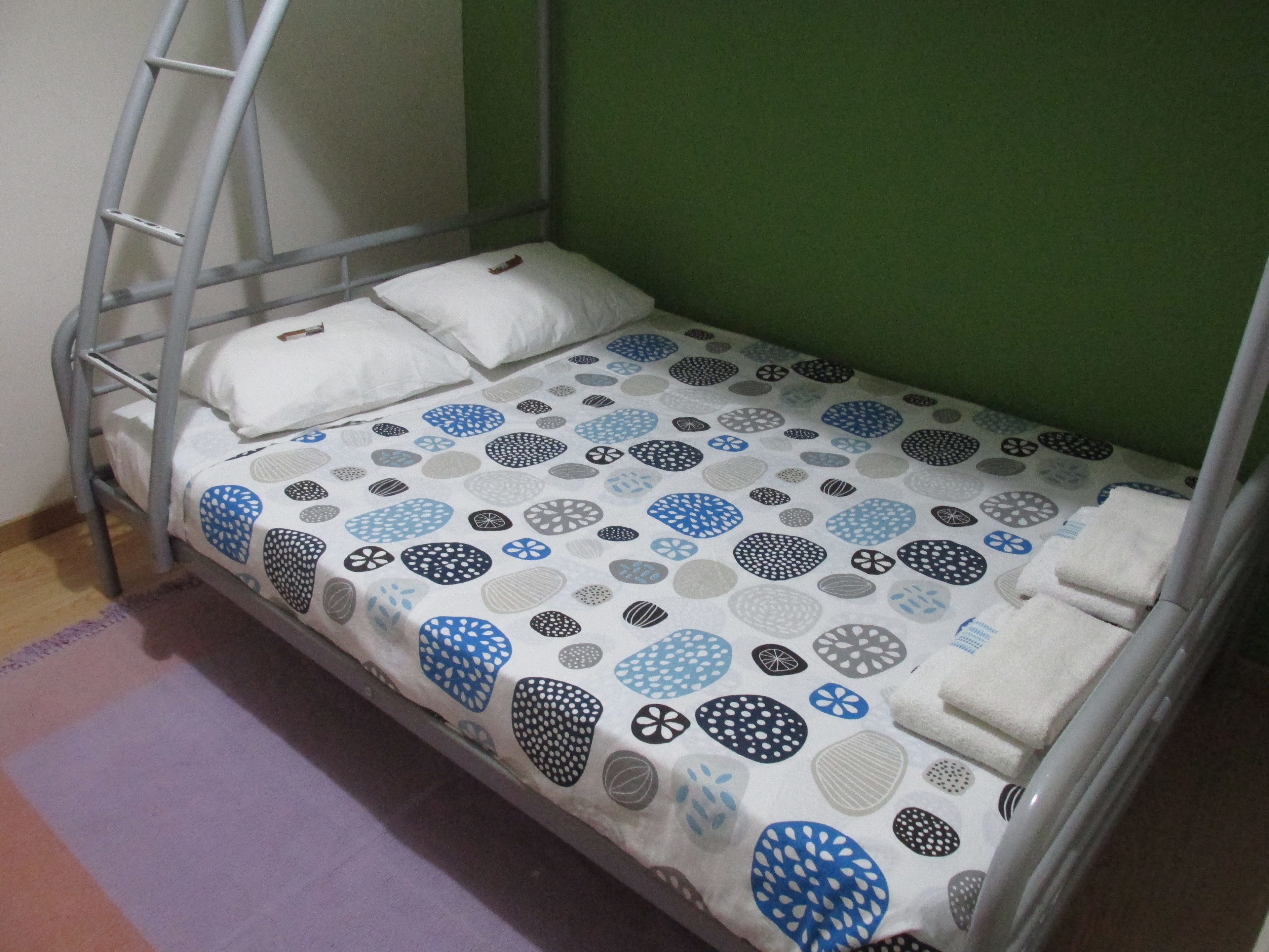 Cama de solteiro com estrutura de metal, almofadas brancas e colcha estampada.
