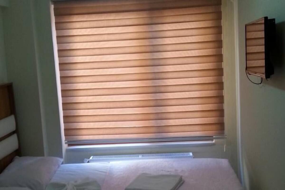 Quarto com cama, janela com persianas horizontais e televisão na parede.