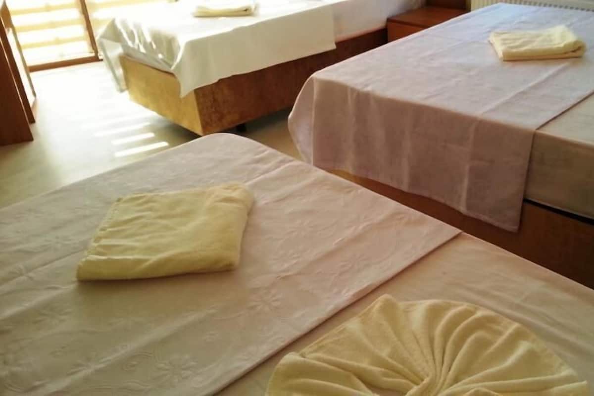 Quarto de hotel com três camas, cada uma com um cobertor dobrado e um travesseiro.