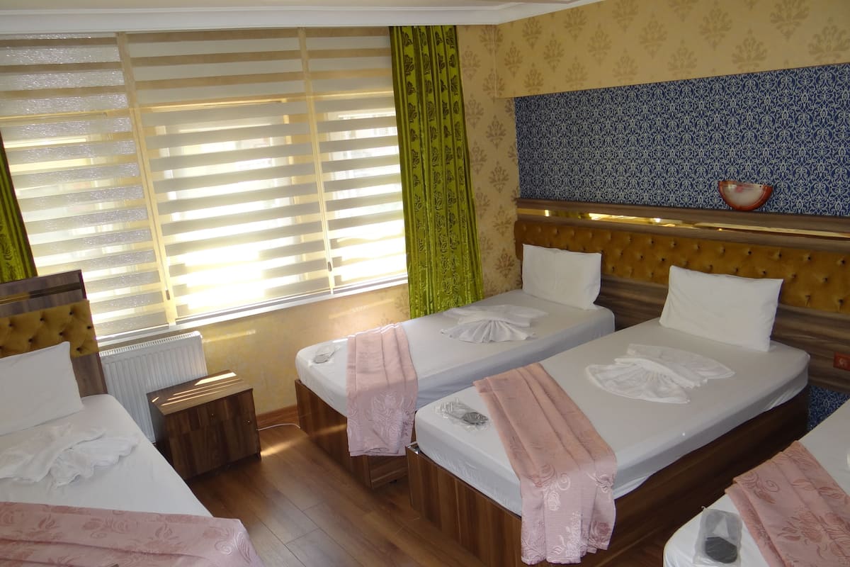 Quarto de hotel com duas camas, cabeceiras de madeira, um radiador, uma janela com persianas e um papel de parede estampado.