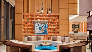 Um lobby moderno com área de estar central, estantes de madeira com objetos decorativos e um balcão de recepção de mármore.