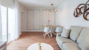 Uma sala de estar moderna com sofá, mesa de jantar com cadeiras, mesa de centro com planta e um detalhe decorativo na parede.
