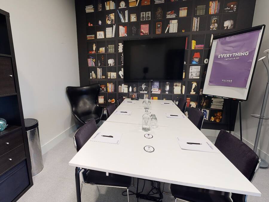 Uma sala de conferências com uma longa mesa branca, cadeiras pretas, uma estante com diversos objetos e uma tela exibindo 'EVERYTHING'.