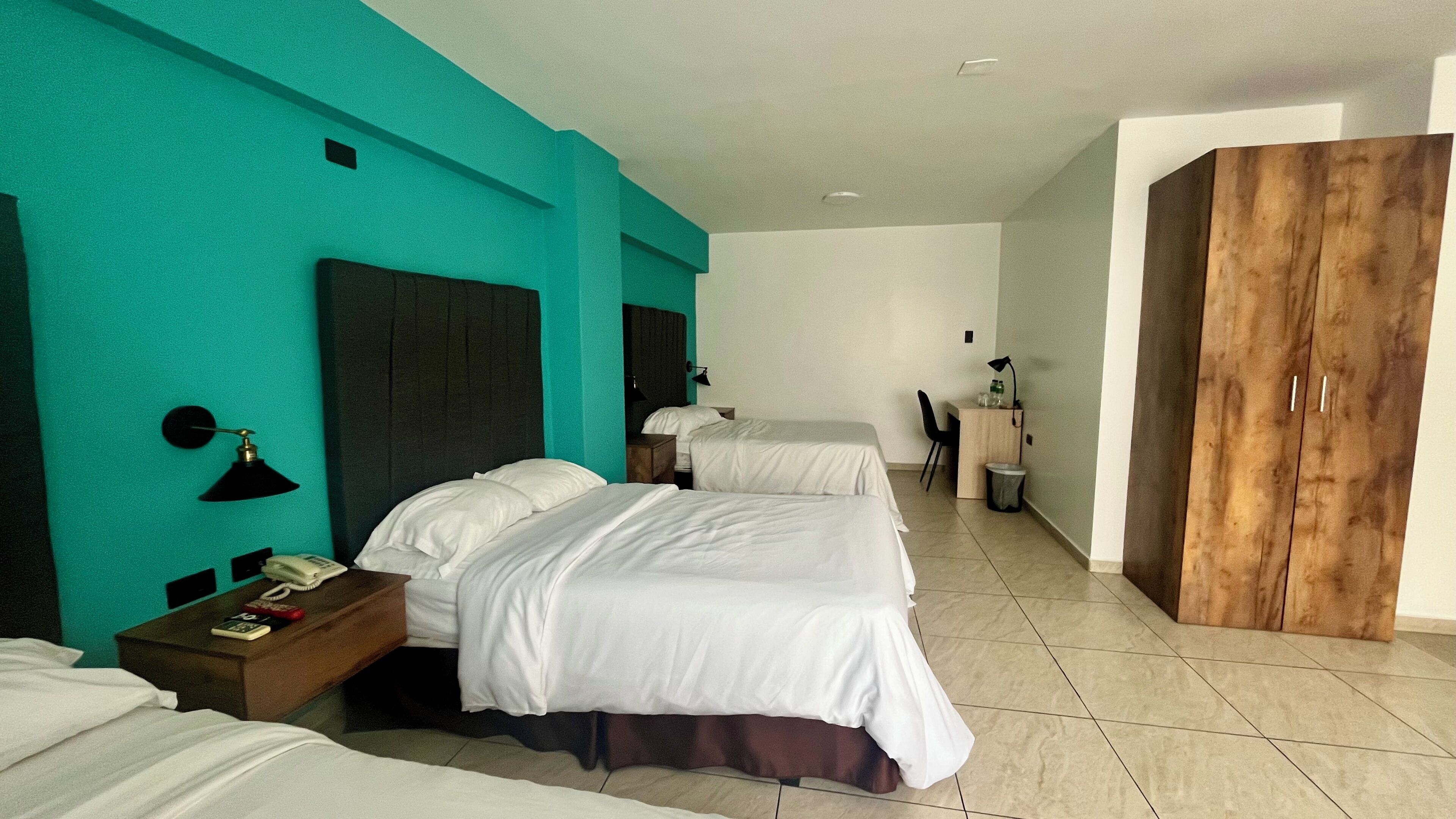 Quarto de hotel com duas camas, uma escrivaninha, um guarda-roupa e um banheiro.