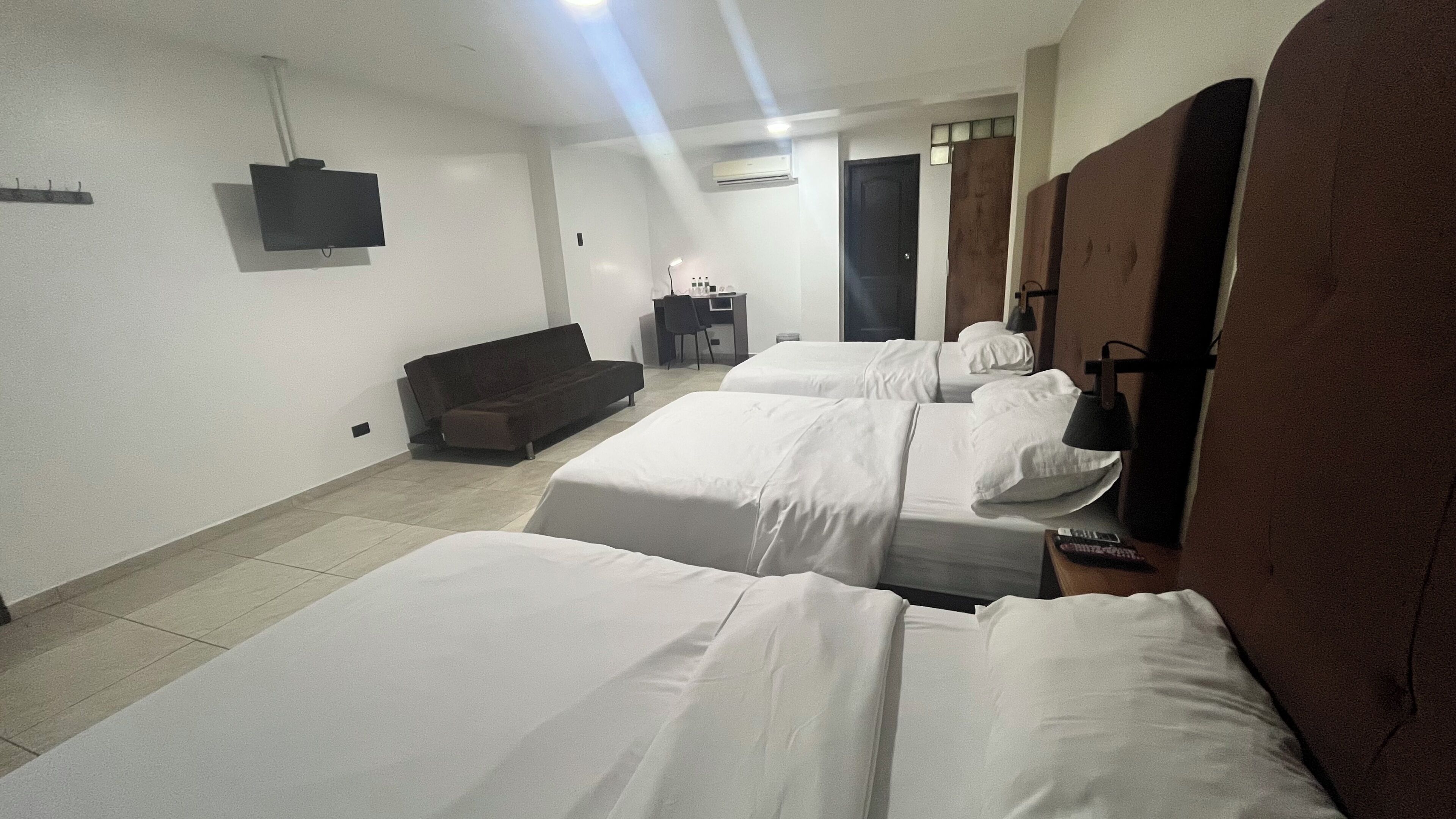 Quarto de hotel com três camas, um sofá, uma escrivaninha e uma televisão.