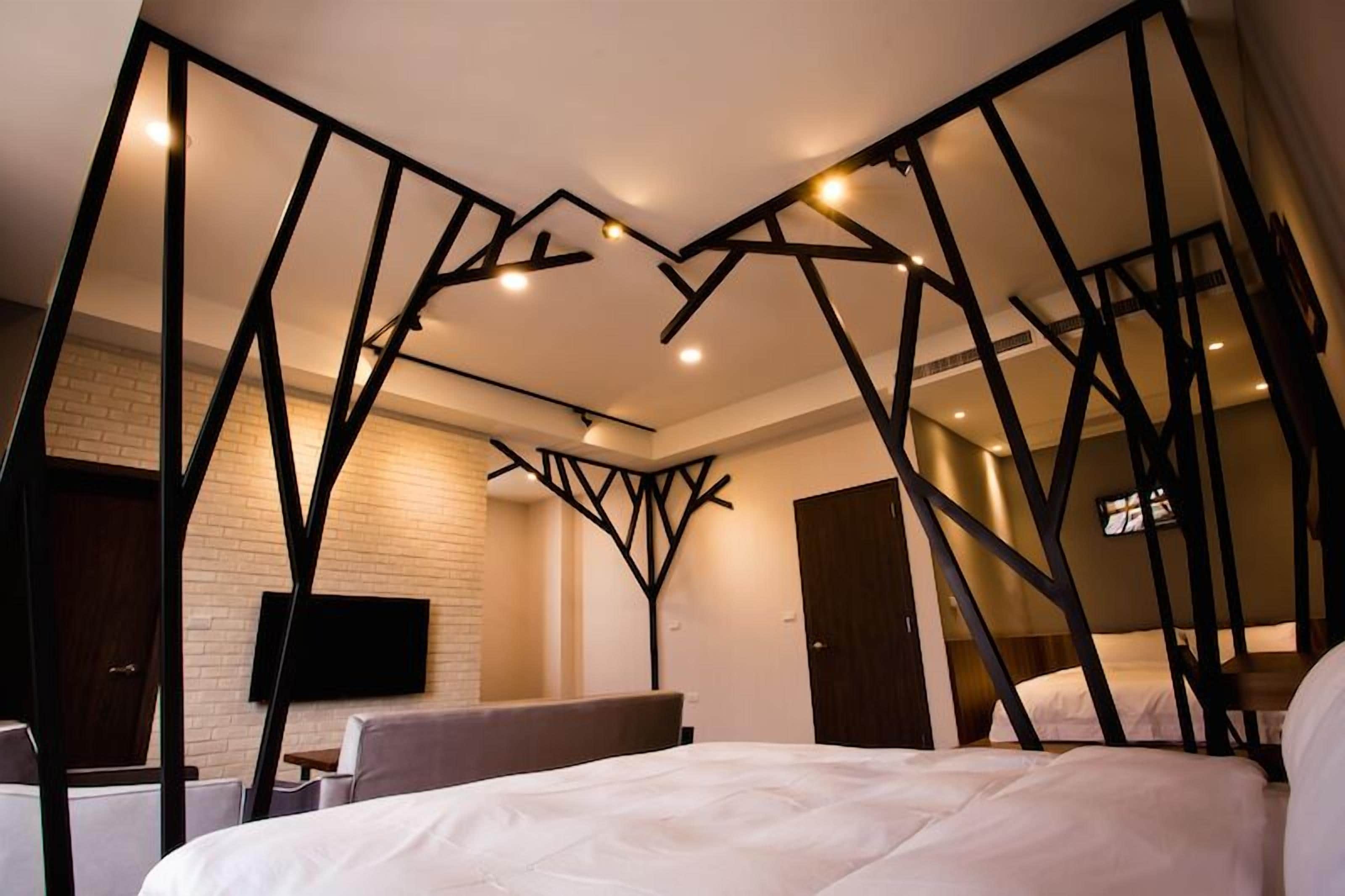 Quarto de hotel moderno com design geométrico no teto, televisão de tela plana na parede e cama com roupa de cama branca.