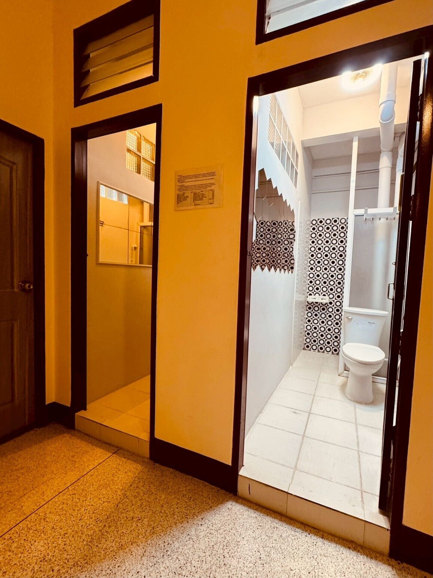 Um corredor com uma porta que dá para um banheiro, com vaso sanitário e chuveiro.