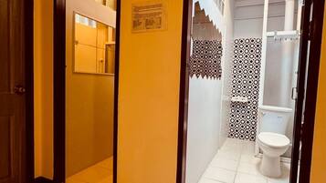 Um corredor com uma porta que dá para um banheiro, com vaso sanitário e chuveiro.