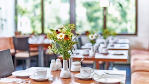 Uma área de refeições com mesas preparadas para o café da manhã, incluindo pratos, xícaras e um vaso de flores.