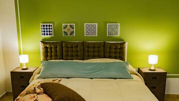 Uma cama bem arrumada com cabeceira verde, duas mesas de cabeceira com abajures e quatro objetos decorativos fixados na parede.