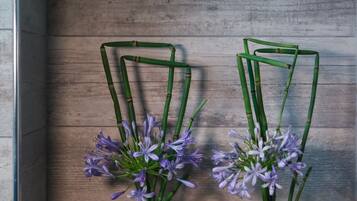 Dois vasos de vidro com flores roxas e caules verdes sobre uma prateleira de madeira.