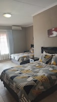 Quarto de hotel com duas camas, uma janela com cortinas, uma luminária no teto e um ar-condicionado fixado na parede.
