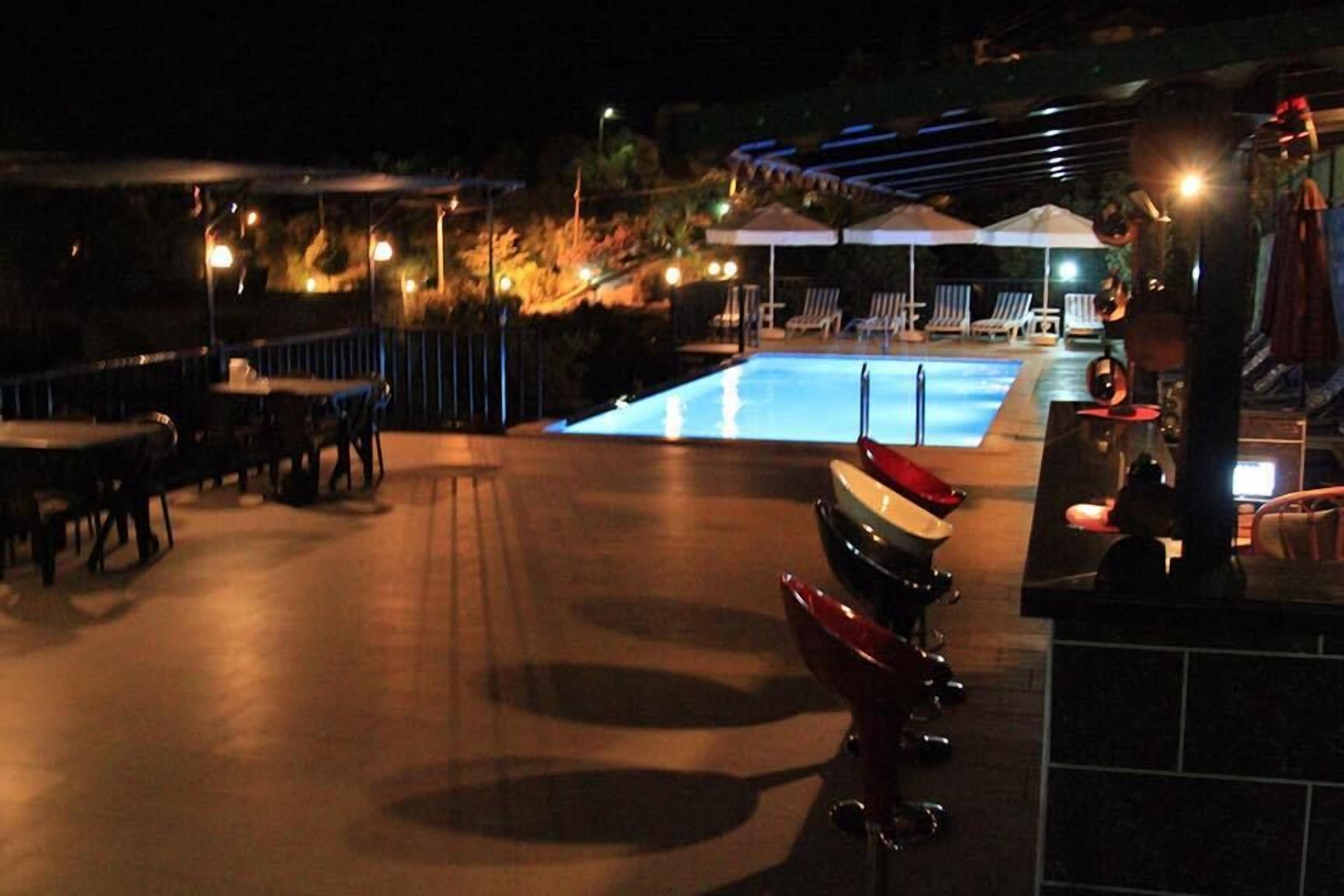 Área de piscina ao ar livre à noite, com espreguiçadeiras e guarda-sóis.