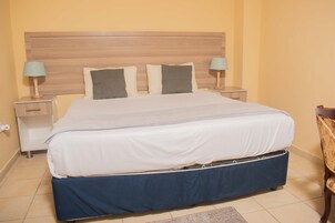 Quarto de hotel com uma cama grande, duas mesas de cabeceira com luminárias, uma cabeceira de madeira e uma cadeira.