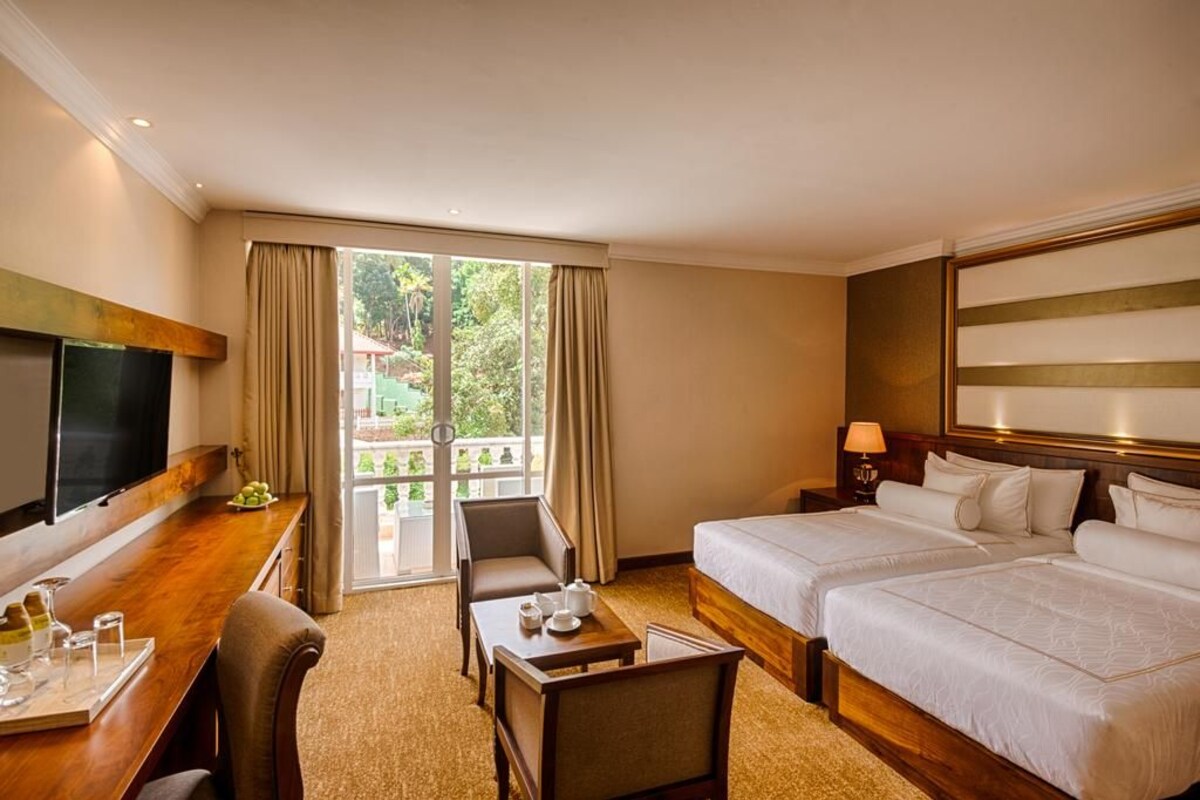 Quarto de hotel com duas camas, uma escrivaninha com cadeira, televisão e vista para o exterior.