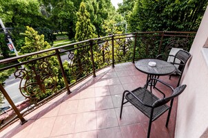 Varanda com mesa e cadeiras, guarda-corpo de metal e vista para árvores e uma estrada.
