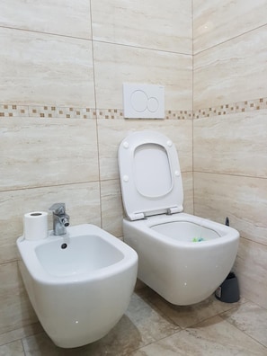 Casa de banho com duas sanitas, um bidé e suporte para papel higiénico.