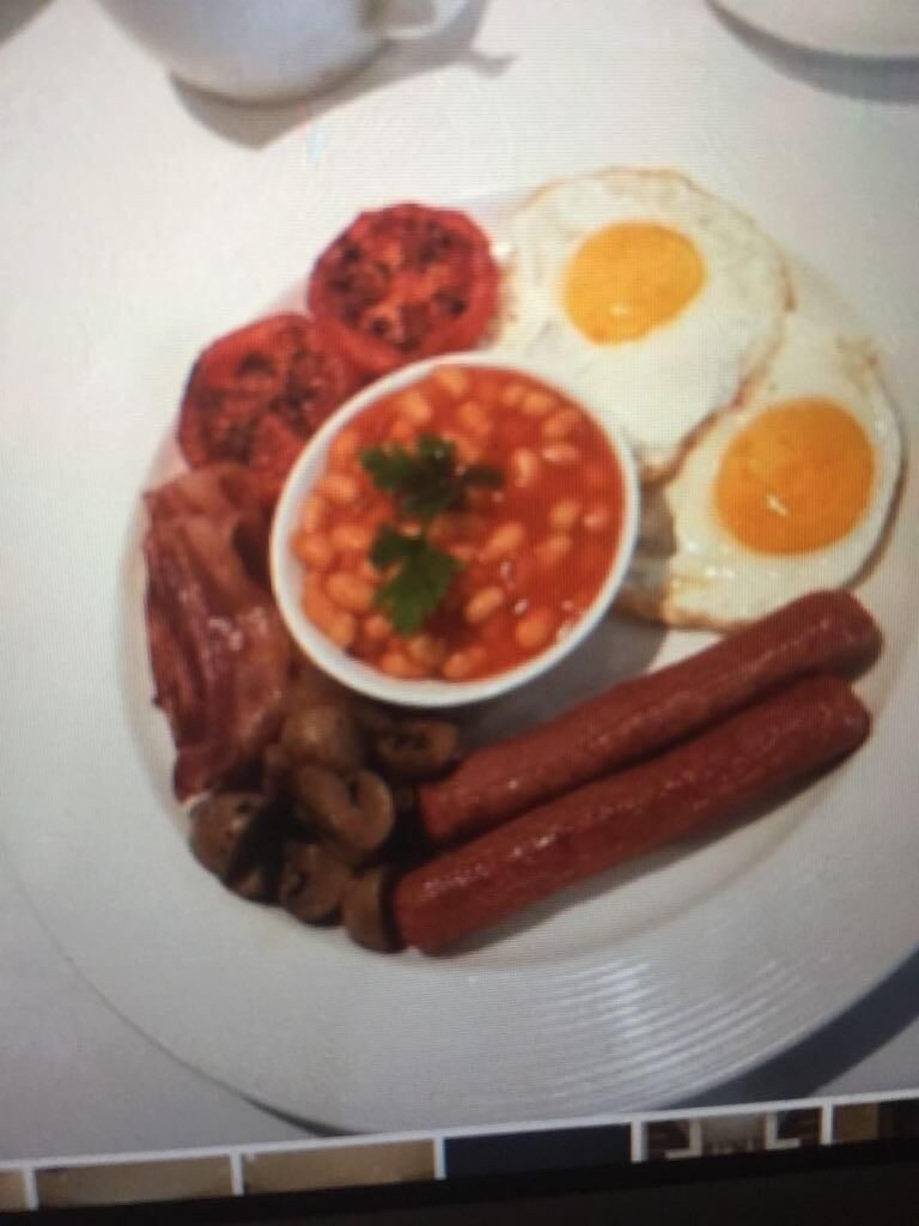 Um prato com ovos, feijão, tomates, linguiça e cogumelos.