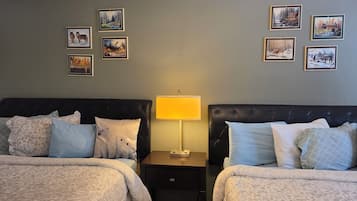 Quarto de hotel com duas camas, uma mesa de cabeceira com abajur e várias fotos emolduradas na parede.