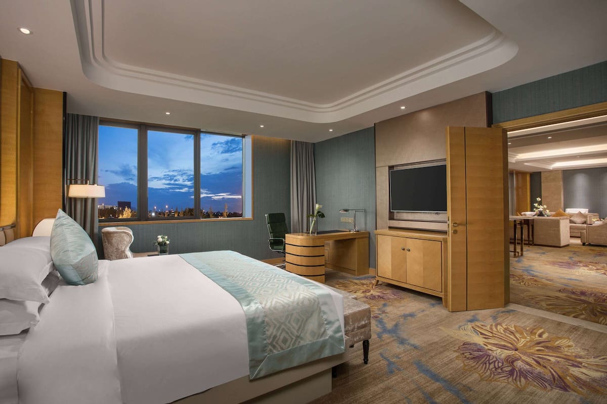 Quarto de hotel com uma cama grande, uma escrivaninha, uma TV e vista para a cidade.