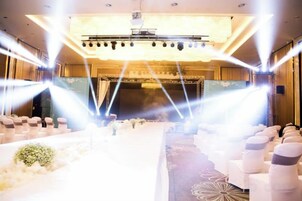 Palco com fileira de cadeiras voltadas para ele, um candelabro acima e piso coberto de carpete.