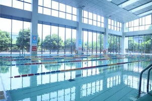 Piscina interna com pistas demarcadas, grandes janelas e vista para árvores do lado de fora.