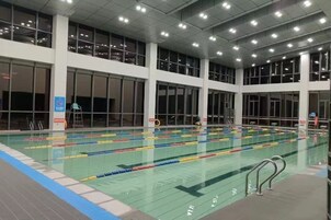 Piscina interna com várias pistas de natação, amplas janelas e piso revestido de azulejos.