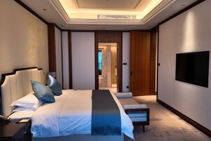 Quarto de hotel com uma cama grande, mesa de cabeceira e televisão na parede.