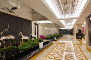Um saguão moderno de hotel com um corredor longo, esculturas decorativas de animais e piso estampado.