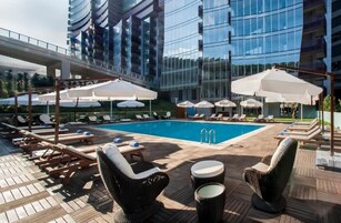 Área de piscina no terraço com espreguiçadeiras, guarda-sóis e vista clara para edifícios modernos.