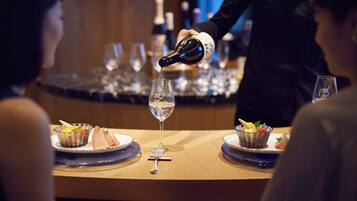 Um bar com alguém servindo uma bebida em um copo, dois pratos com comida e um balcão de bar cheio de copos e garrafas.