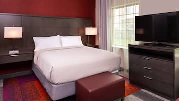 Quarto de hotel com uma cama grande, duas mesas de cabeceira com abajures, uma TV em uma cômoda e uma janela com cortinas.