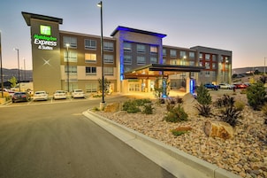 Um hotel Holiday Inn Express & Suites com design moderno, que inclui um estacionamento e área ajardinada com pedras e arbustos.