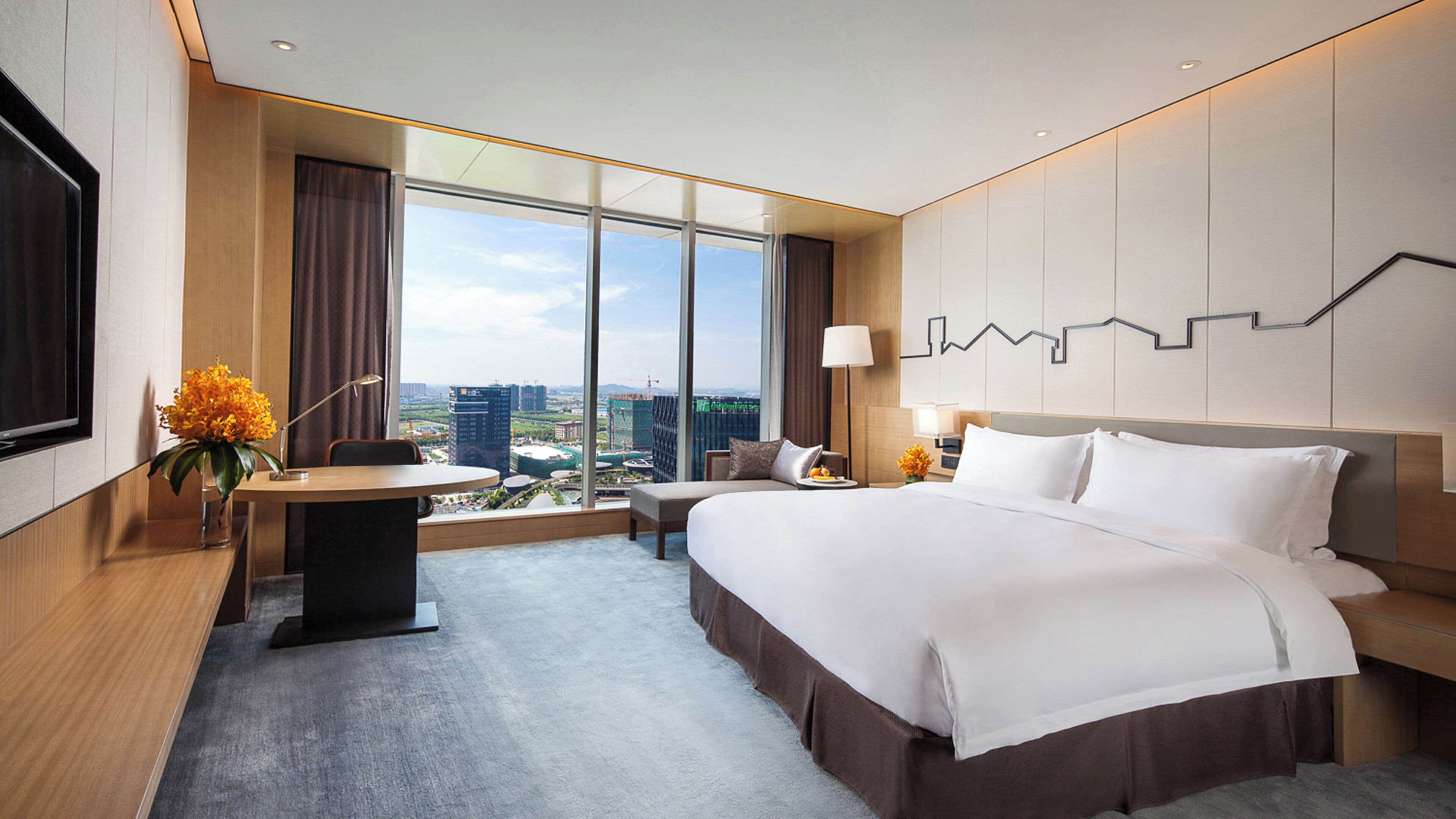 Quarto de hotel com uma cama grande, uma escrivaninha, uma cadeira, uma televisão e vista para a cidade.