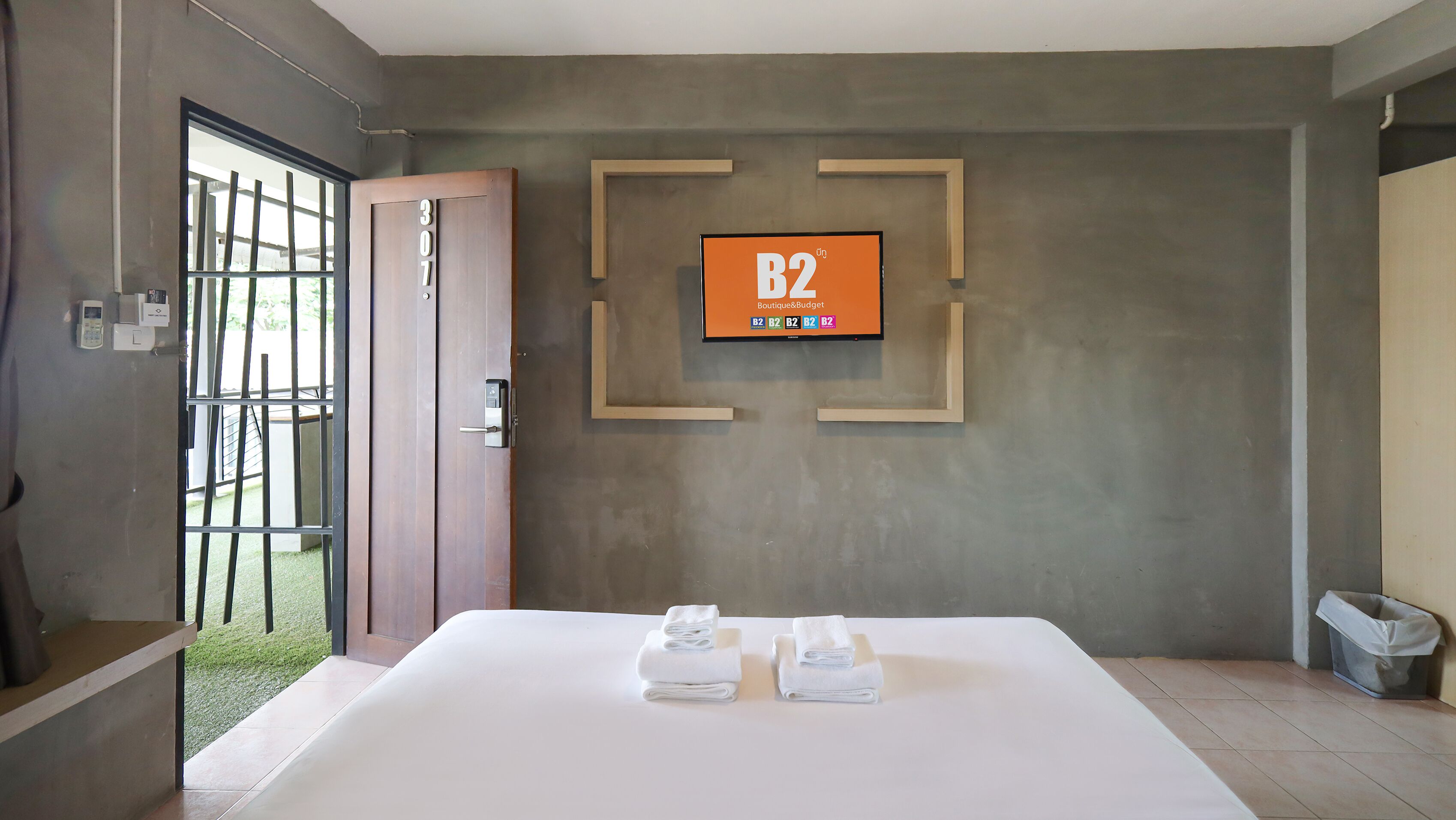 Quarto de hotel com cama, televisão fixada na parede e vista para o exterior através de uma porta.