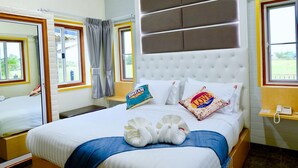 Quarto de hotel com uma cama grande, uma mesinha de cabeceira, um espelho e uma janela com cortinas.