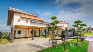 Uma casa moderna de dois andares com varanda coberta, um pequeno jardim com árvores bem aparadas e um céu azul límpido.