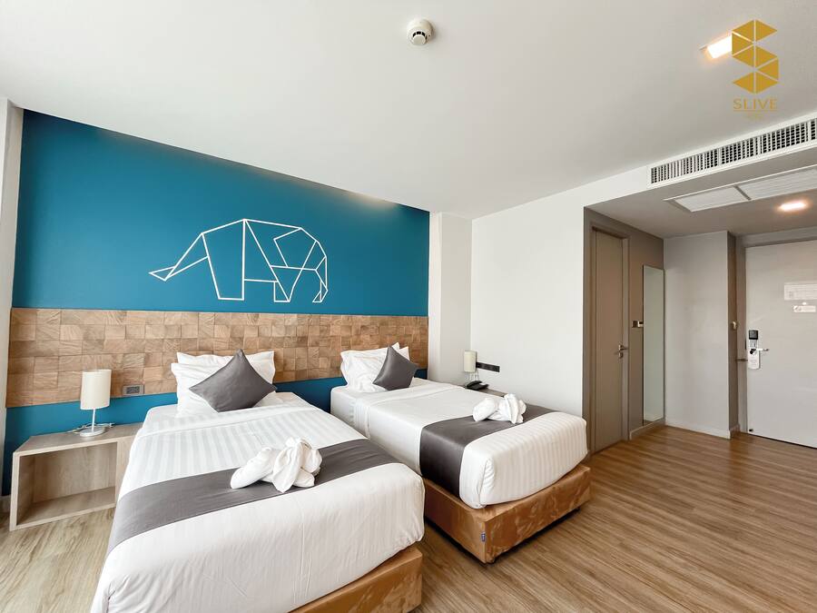Quarto de hotel com duas camas, uma parede azul de destaque e uma obra de arte geométrica na parede.