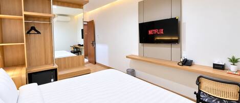 Quarto de hotel com cama, guarda-roupa, secretária com computador, televisão e cadeira.
