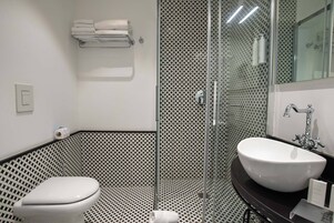 Casa de banho com sanita, chuveiro com porta de vidro e lavatório com espelho.