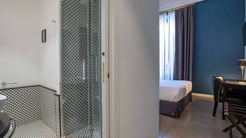 Quarto de hotel com chuveiro, cama, escrivaninha e cadeira.