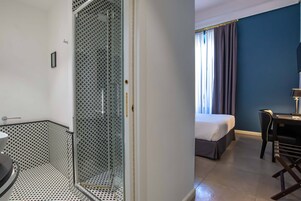 Quarto de hotel com chuveiro, cama, escrivaninha e cadeira.