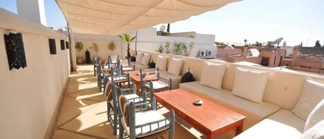 Terraço ao ar livre com sofá, cadeiras e mesa sob um toldo.