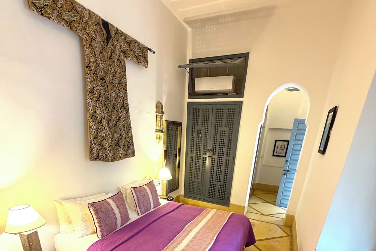 Um quarto com uma cama, mesa de cabeceira, luminária, cadeira e guarda-roupa.