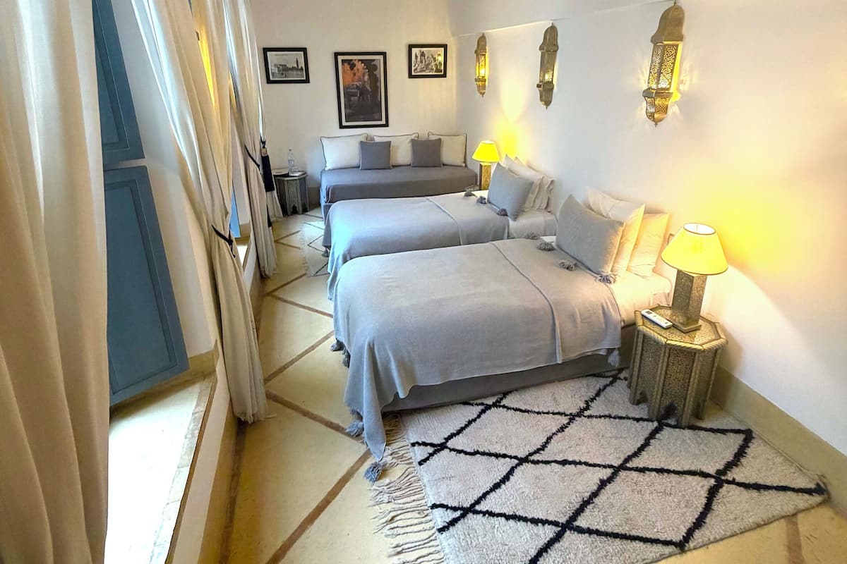 Quarto de hotel com duas camas, uma mesinha, luminárias fixadas na parede e um tapete estampado.
